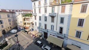 Um edifício com vários andares, varandas, um café no térreo e uma área de estacionamento.