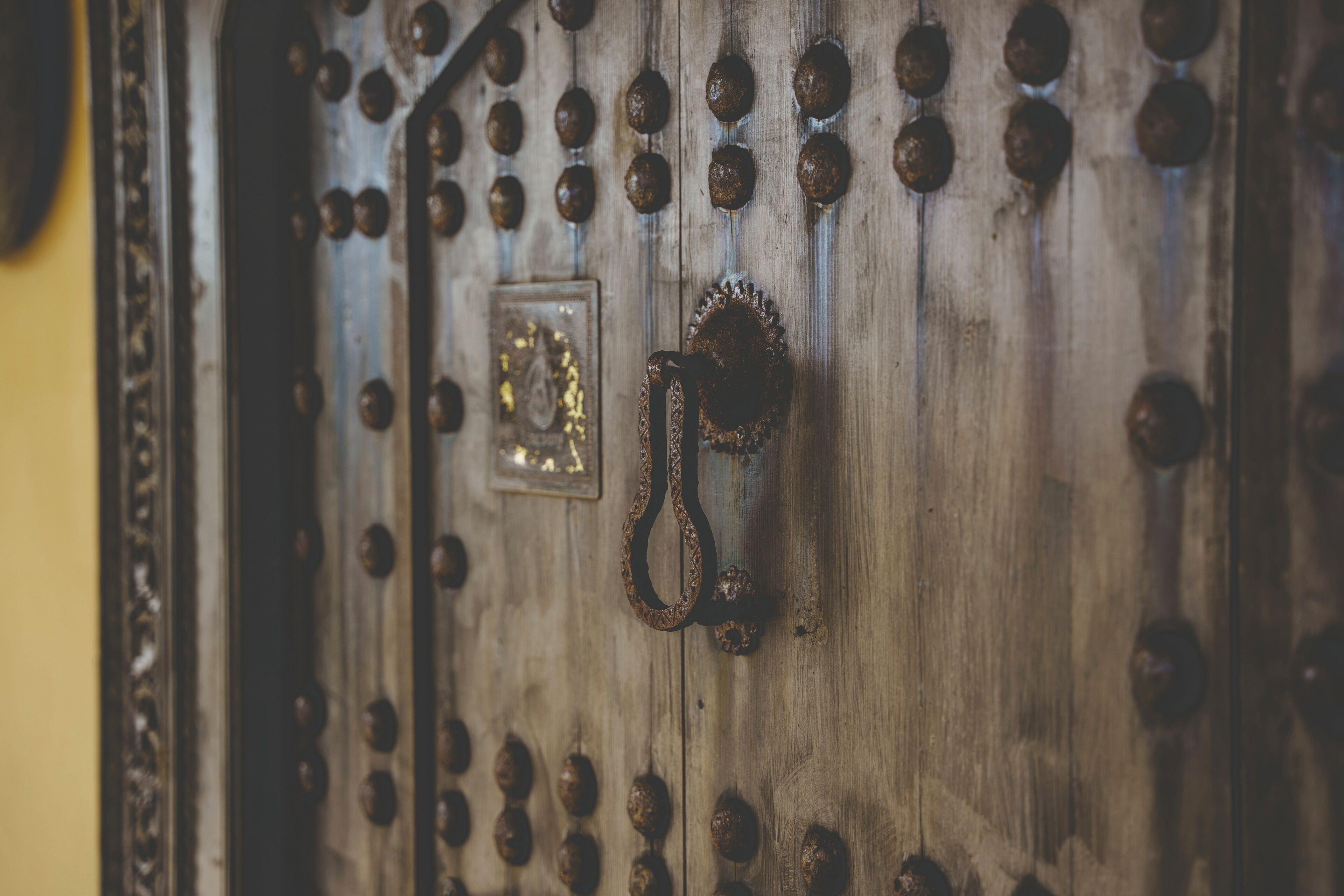 Uma porta de madeira com rebites metálicos e uma maçaneta decorativa de metal.