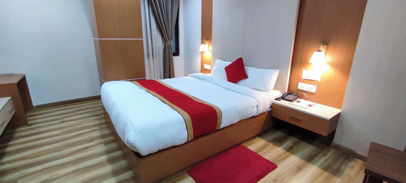 Quarto de hotel com cama, mesa de cabeceira, abajur e um tapete vermelho.