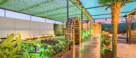 Uma área de jardim coberta com um caminho de madeira, vasos de plantas e um arco floral decorativo.