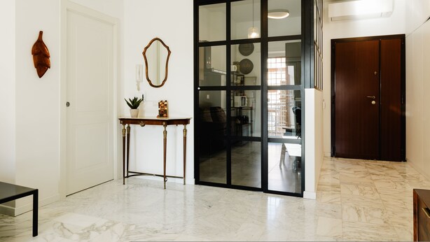 Um corredor amplo com piso de mármore, porta de madeira, porta de vidro que dá para uma cozinha e um guarda-roupa de madeira.