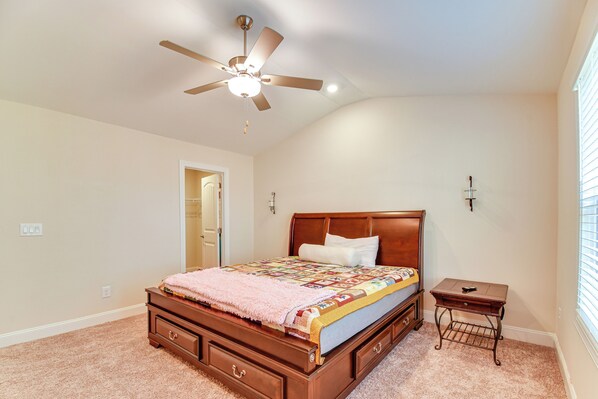 Quarto com cama de madeira, ventilador de teto, mesa de cabeceira e janela com persianas.