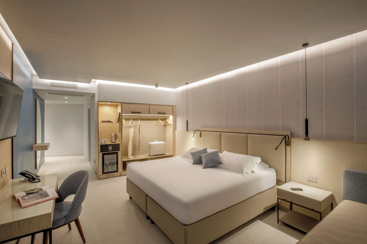 Quarto de hotel moderno com uma cama grande, mesas de cabeceira, escrivaninha e guarda-roupa.
