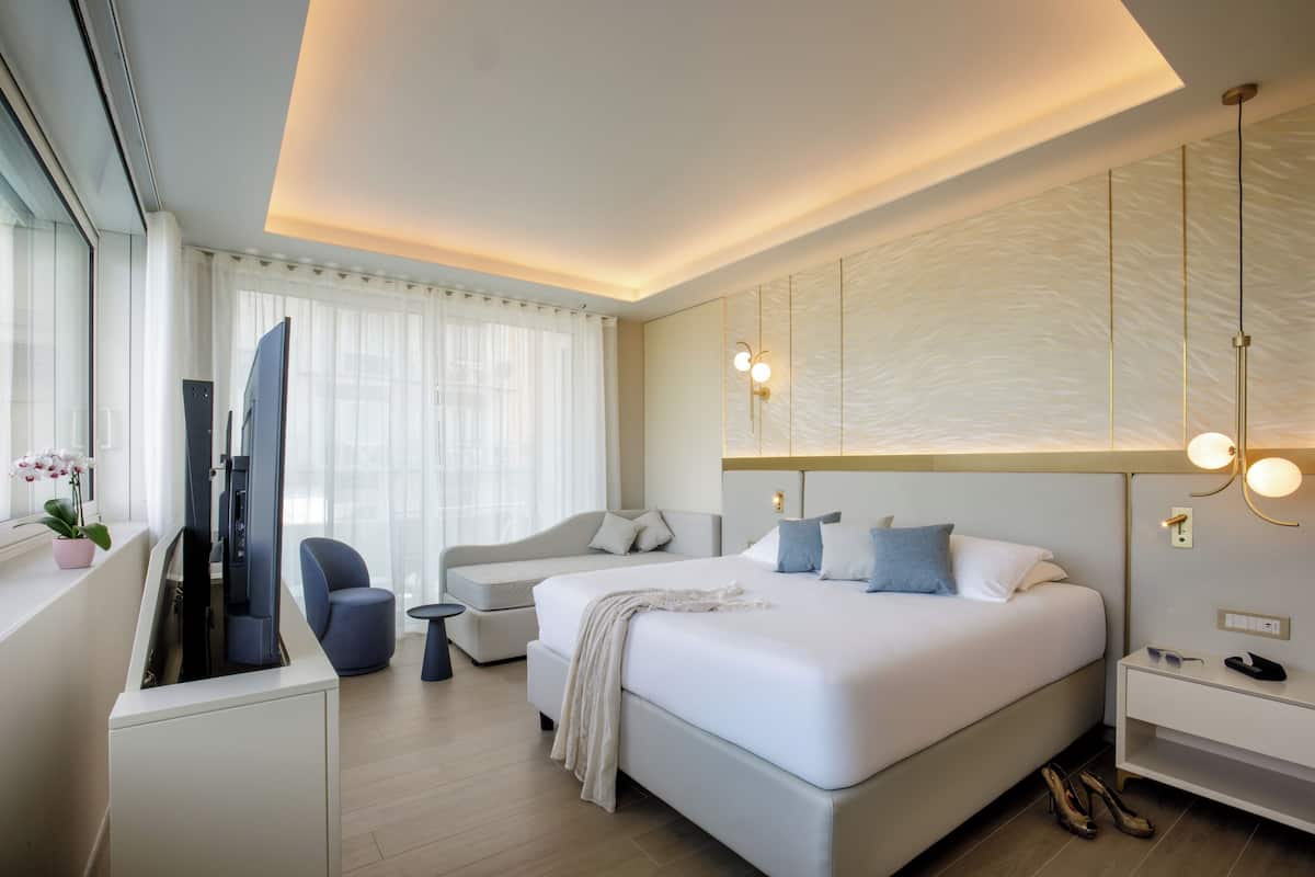 Quarto de hotel moderno com uma cama grande, um sofá, uma televisão e uma escrivaninha.