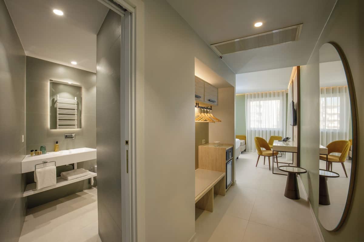 Casa de banho moderna com toucador, suporte de toalhas e espelho. Zona de refeições com cadeiras amarelas e uma mesa.