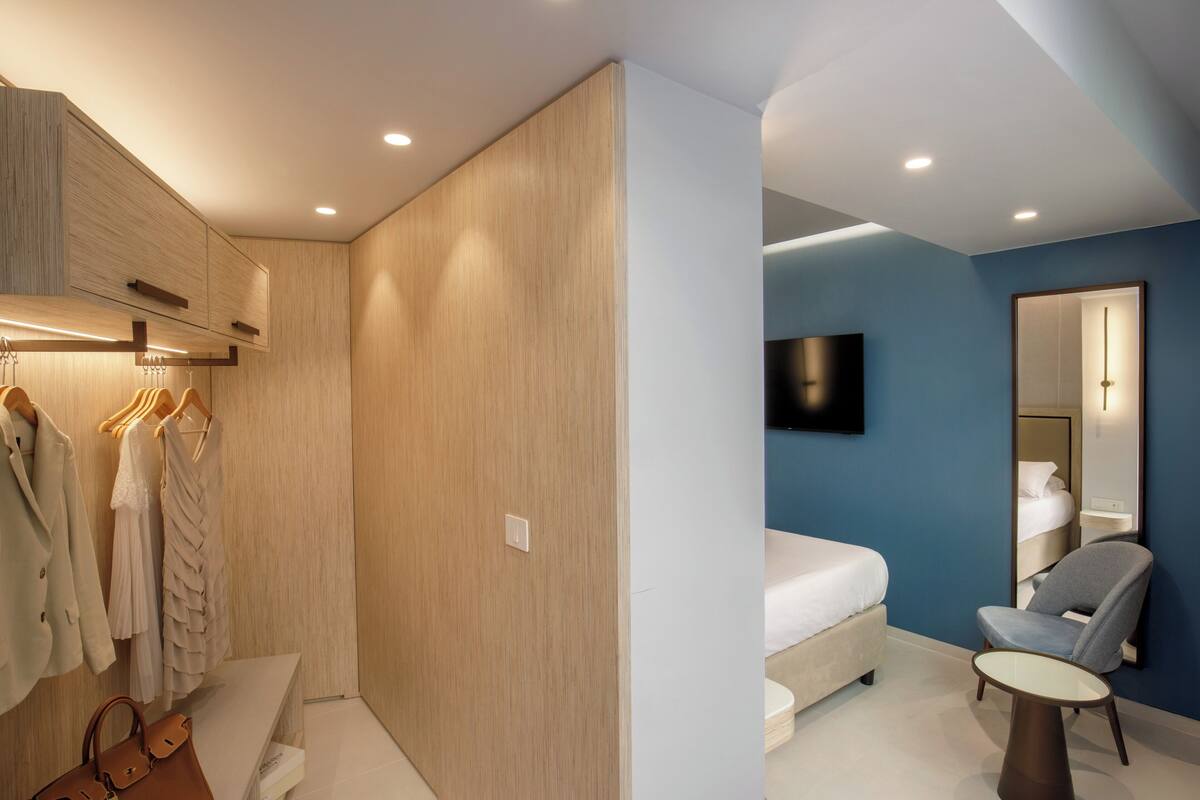 Quarto de hotel moderno com um guarda-roupa de madeira, uma cama, uma televisão e uma cadeira.