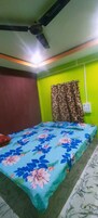 Quarto com cama, ventilador de teto, parede verde e janela com cortinas.