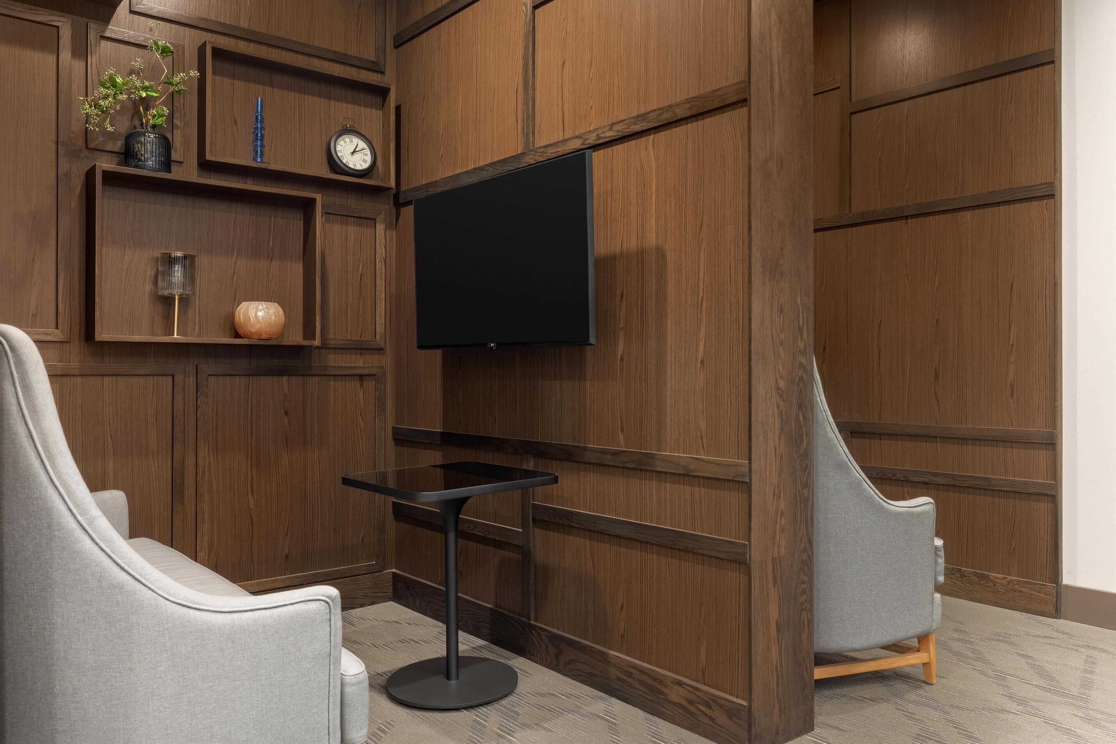 Quarto moderno com parede de painel de madeira, TV de tela plana presa acima de uma mesa preta e poltrona cinza.