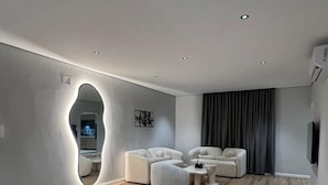 Sala de estar moderna com piso de madeira, um espelho grande e uma área de estar com sofás e uma mesa de centro.