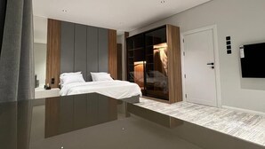 Quarto moderno com cama grande, roupeiro embutido e televisão de tela plana na parede.