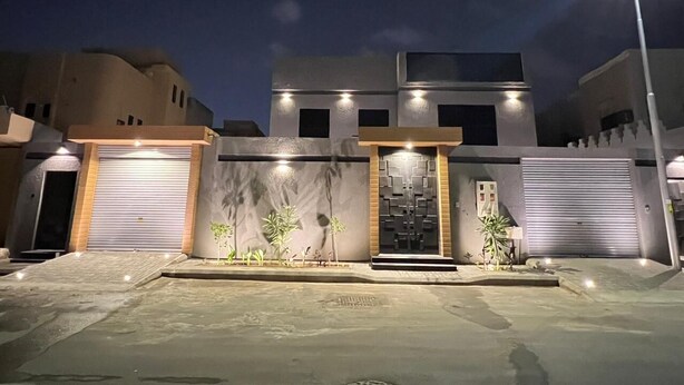 Um edifício moderno com duas portas de garagem, uma pequena entrada com degraus e uma entrada bem iluminada à noite.