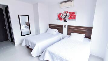 Quarto de hotel com duas camas, um espelho grande e ar condicionado fixado na parede.