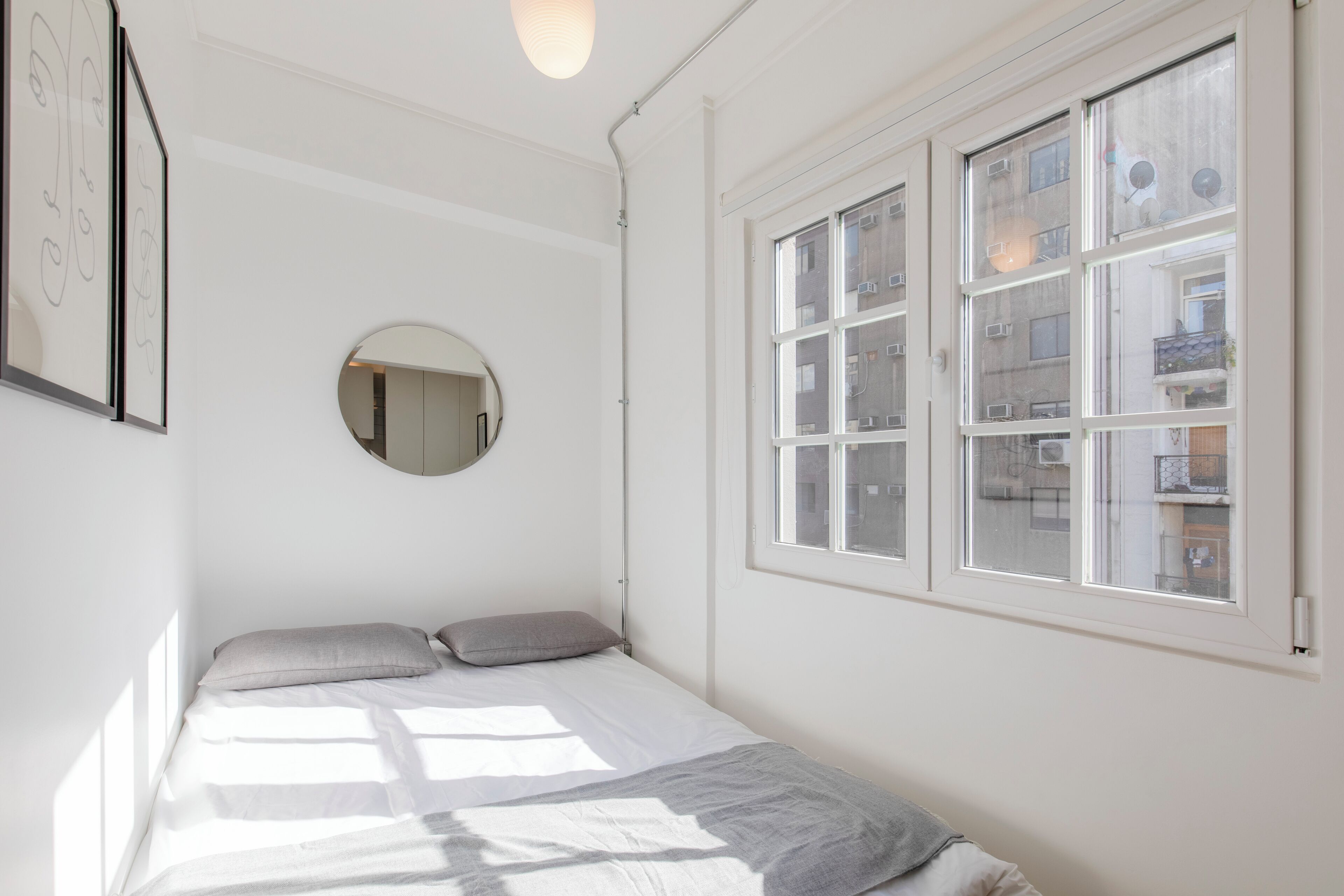Quarto com cama, espelho redondo e janela com vários painéis.