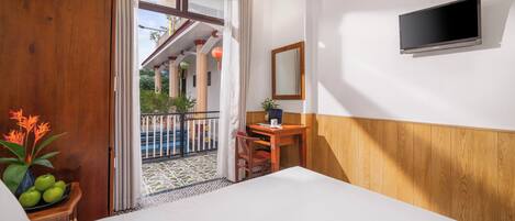 Quarto de hotel com cama, escrivaninha, televisão e varanda com vista exterior.