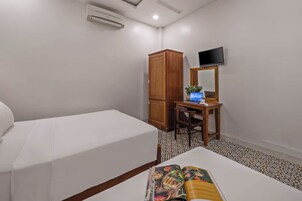 Quarto de hotel com uma cama, uma escrivaninha com um laptop, um espelho e um guarda-roupa.