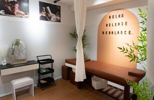 Um quarto de spa com uma mesa de massagem, um banco branco, uma prateleira preta e uma placa na parede com os dizeres 'RELAX RELEASE REDUCE'.