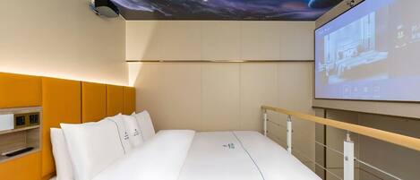 Quarto de hotel com cama, painel de controle, tela exibindo a disposição do quarto e teto com um mural temático do espaço.