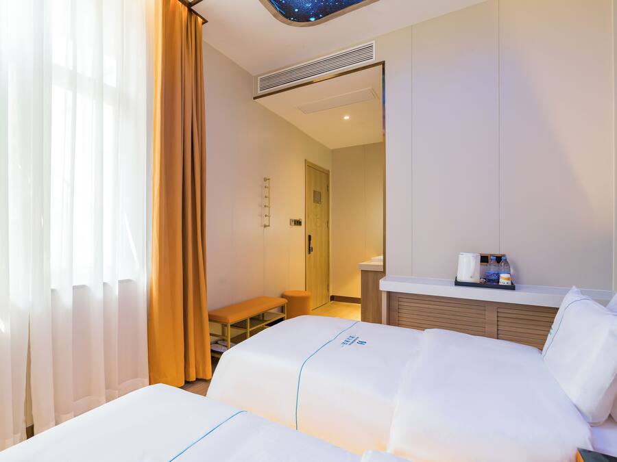 Quarto de hotel com duas camas, um banco, uma mesinha e uma pequena cozinha.