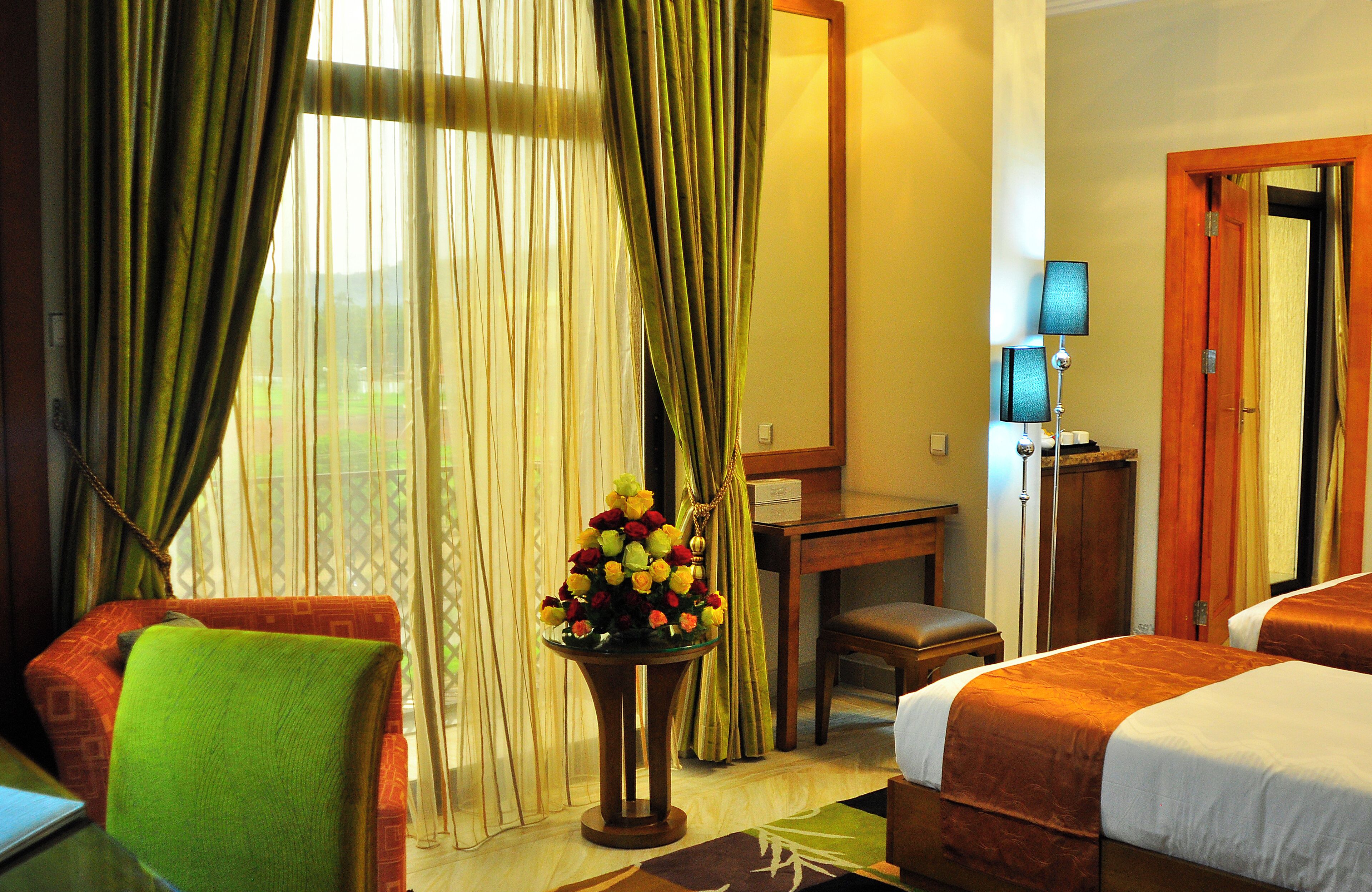 Quarto de hotel com uma cama, uma escrivaninha, uma cadeira e uma mesa com um vaso de flores.