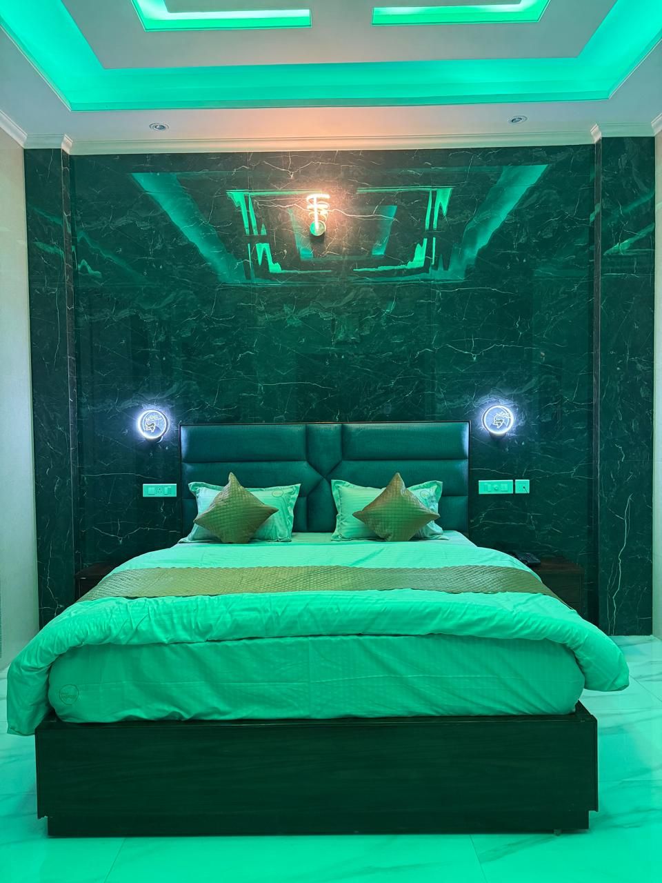 Quarto moderno com design em tons de verde, apresentando uma cama com cabeceira, duas luminárias fixadas na parede e um painel de parede com padrão marmorizado.