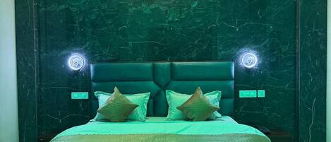 Quarto moderno com design em tons de verde, apresentando uma cama com cabeceira, duas luminárias fixadas na parede e um painel de parede com padrão marmorizado.