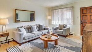 Uma sala de estar com sofá, poltrona, mesa de centro, luminária e um espelho grande.