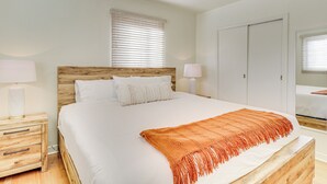 Quarto bem arrumado com uma cama grande, cabeceira de madeira, duas mesas de cabeceira com abajures, ventilador de teto e um guarda-roupa.