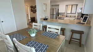 Cozinha moderna com ilha central, armários brancos e área de jantar com mesa e cadeiras de madeira.