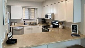 Cozinha com armários brancos, ilha central com banquetas, janela com persianas e placa indicando disponibilidade de Wi-Fi.