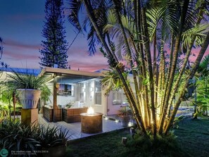 Uma casa moderna com um alpendre coberto, lareira e plantas tropicais exuberantes.