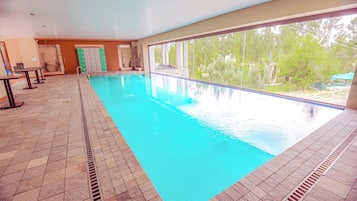 Piscina com chão em mosaico e vista para árvores.
