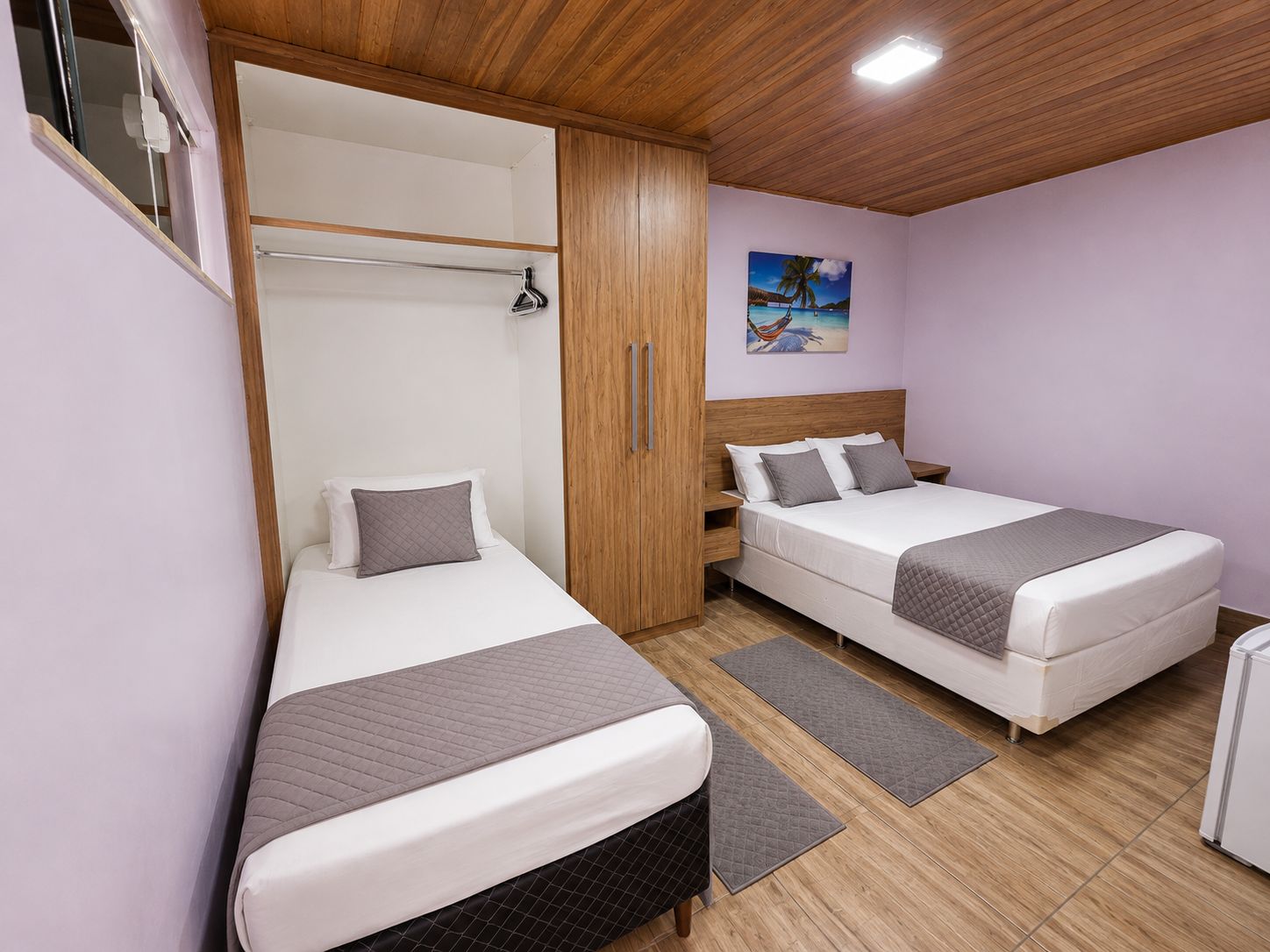 Quarto com duas camas, um guarda-roupa, um quadro e teto de madeira.