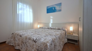 Quarto com cama, duas mesas de cabeceira, um criado-mudo, janela com cortinas e um quadro na parede.