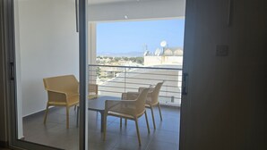 Uma varanda com cadeiras de vime e uma mesa, com vista para a paisagem urbana e montanhas.