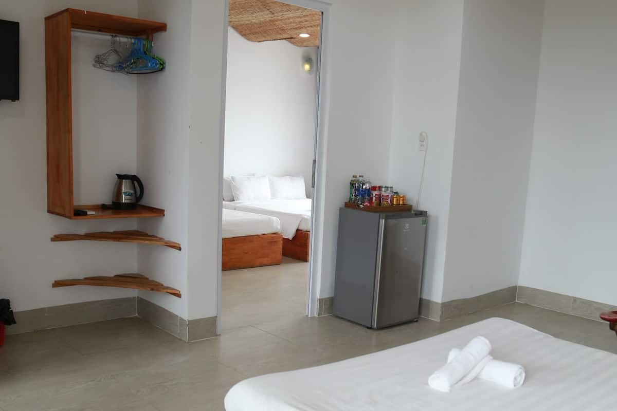Quarto com uma cama grande, uma prateleira de madeira, um pequeno frigorífico e uma porta que dá para outro espaço.
