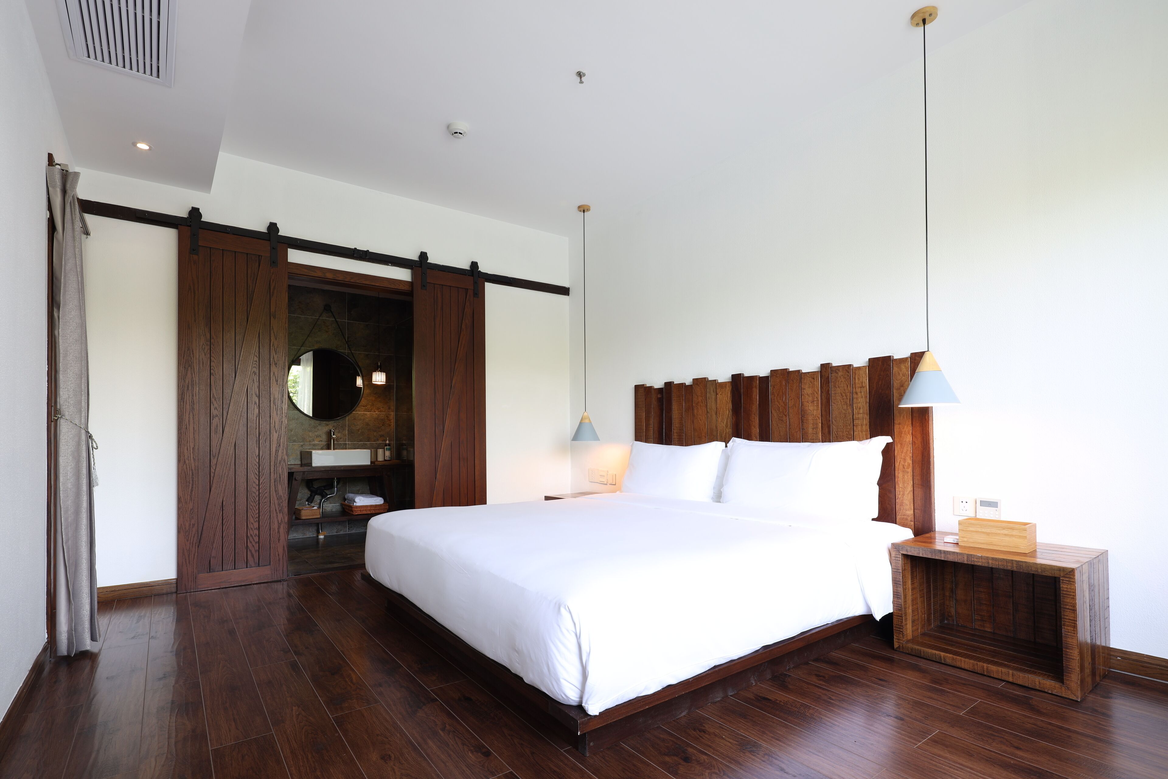 Quarto com uma cama grande, cabeceira de madeira, mesa de cabeceira com abajur, guarda-roupa de madeira e banheiro com pia e espelho.