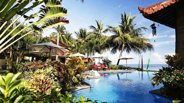 Área de piscina com espreguiçadeiras e guarda-sóis, cercada por palmeiras e plantas tropicais.