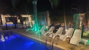 Piscina com um recurso de água azul, rodeada por cadeiras de lounge brancas e um muro de pedra.