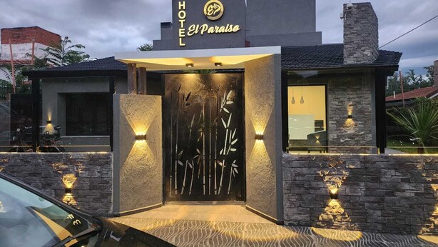 Entrada moderna de um hotel com fachada de pedra, iluminada por luzes embutidas na parede, e uma placa indicando ser o Hotel El Paiso.