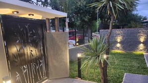 Um edifício moderno com um portão de metal escuro, uma pequena palmeira e iluminação externa.