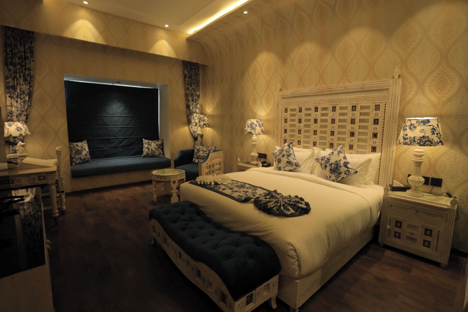Quarto com uma cama grande, área de estar com sofá e uma mesinha, e painel decorativo na parede.