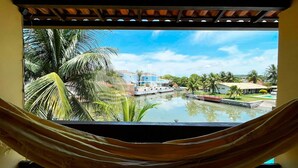 Vista pela janela, mostrando uma rede, piscina, palmeiras e um edifício com telhado azul.