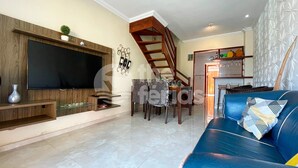 Sala de estar com televisão de tela plana, sofá, área de jantar com cadeiras e um lance de escadas.