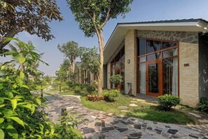 Um edifício moderno com grandes janelas, fachada de pedra e um caminho pavimentado com vegetação.