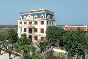 Um edifício com vários andares e varanda no andar superior, rodeado por vegetação.