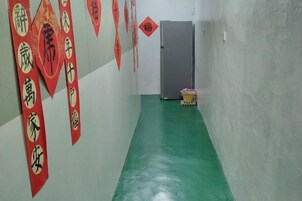 Um corredor com piso verde, uma porta e faixas vermelhas com caracteres chineses.