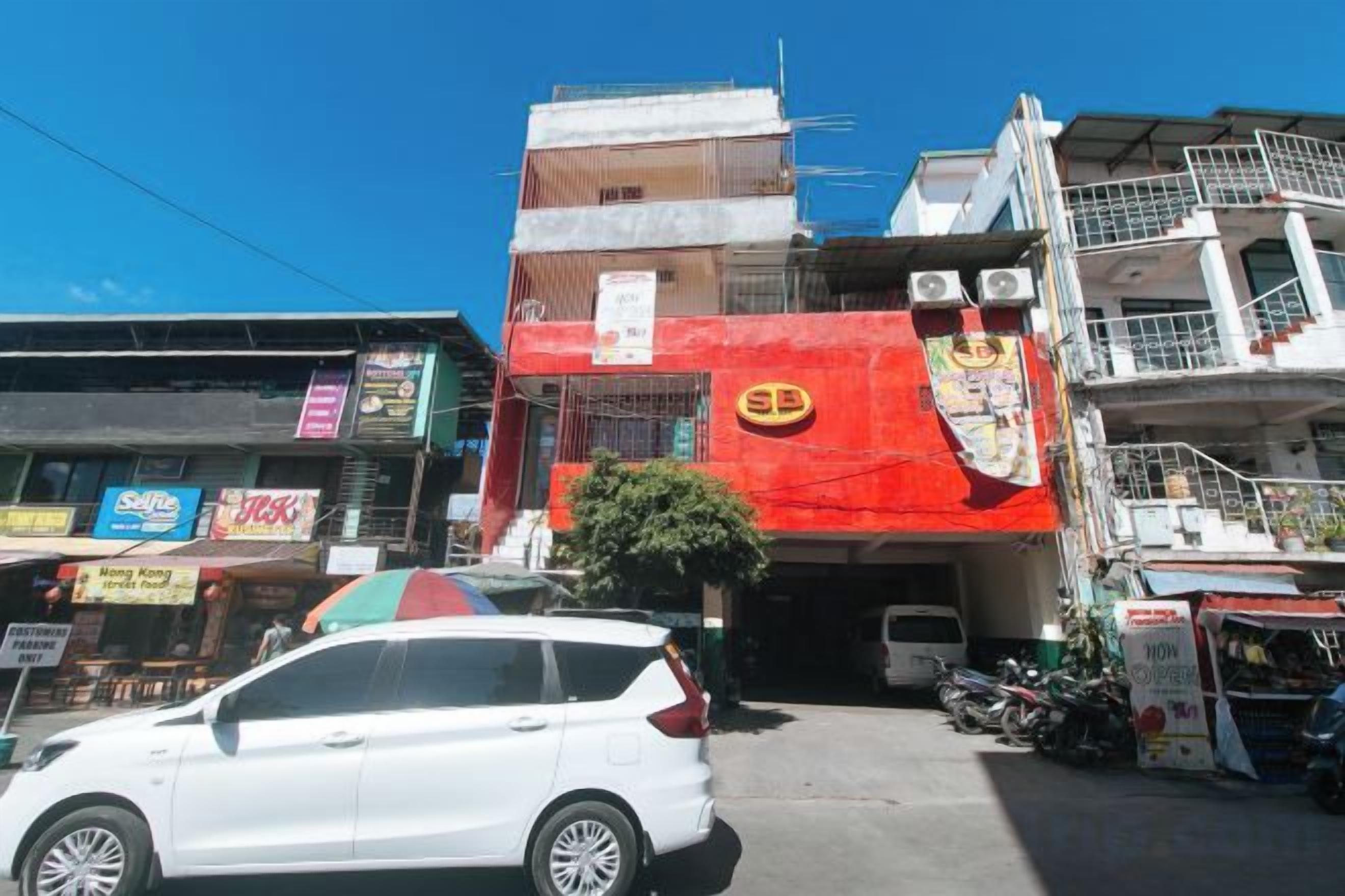Um edifício com várias andares, fachada vermelha, escadaria visível e um carro branco estacionado na frente.