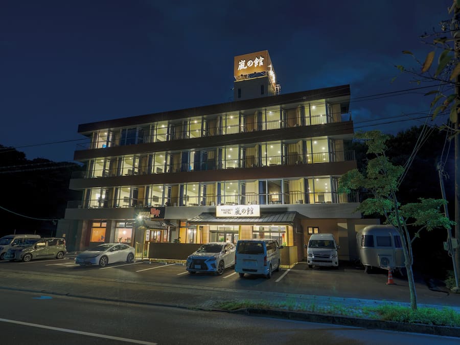 Um hotel de vários andares com uma placa grande, um estacionamento com vários carros e uma van.