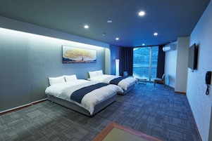 Quarto de hotel com duas camas, uma janela grande com vista, um quadro na parede e uma televisão de tela plana fixada na parede.