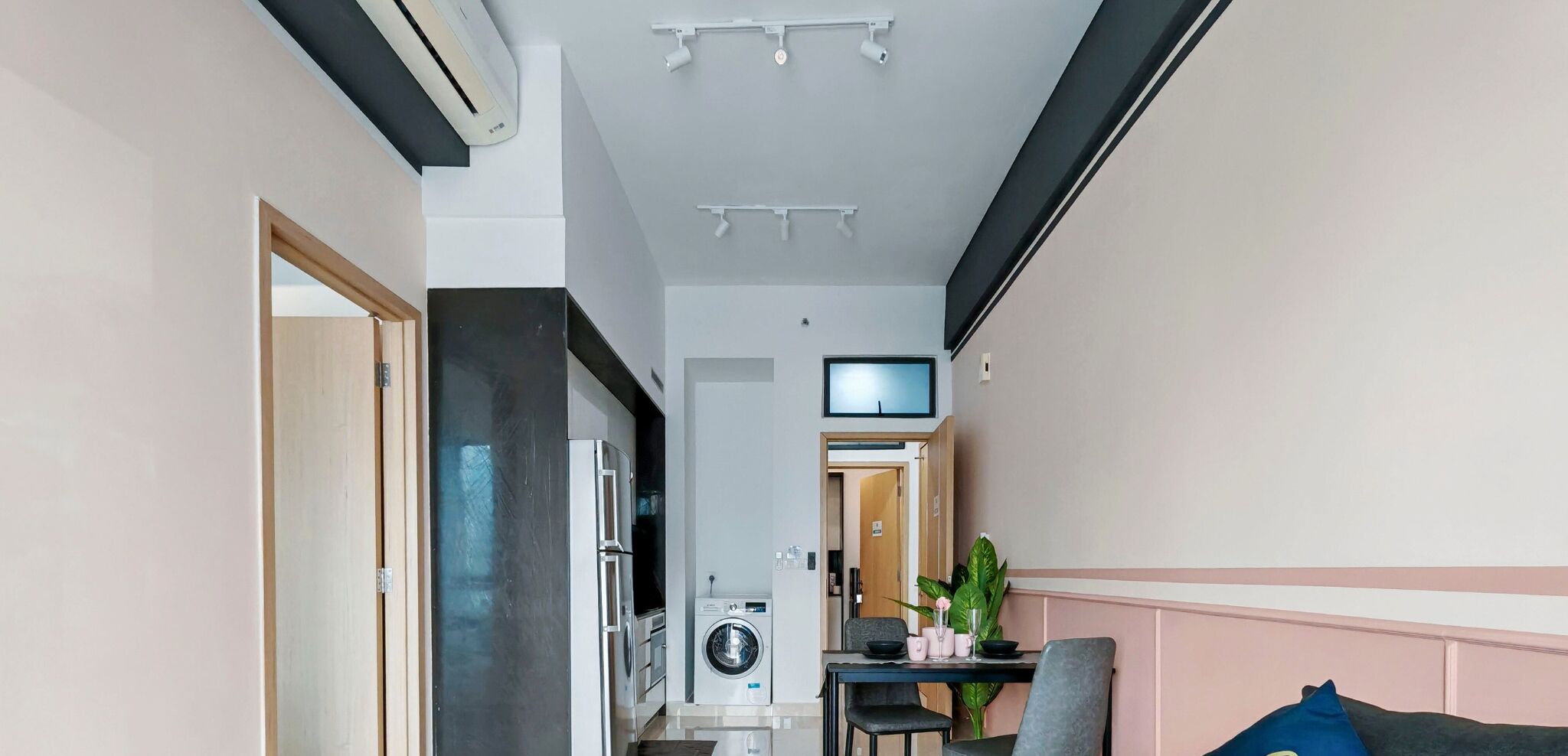 Quarto de hotel moderno com cozinha compacta, televisão de tela plana, máquina de lavar e área de refeições com mesa e cadeiras.